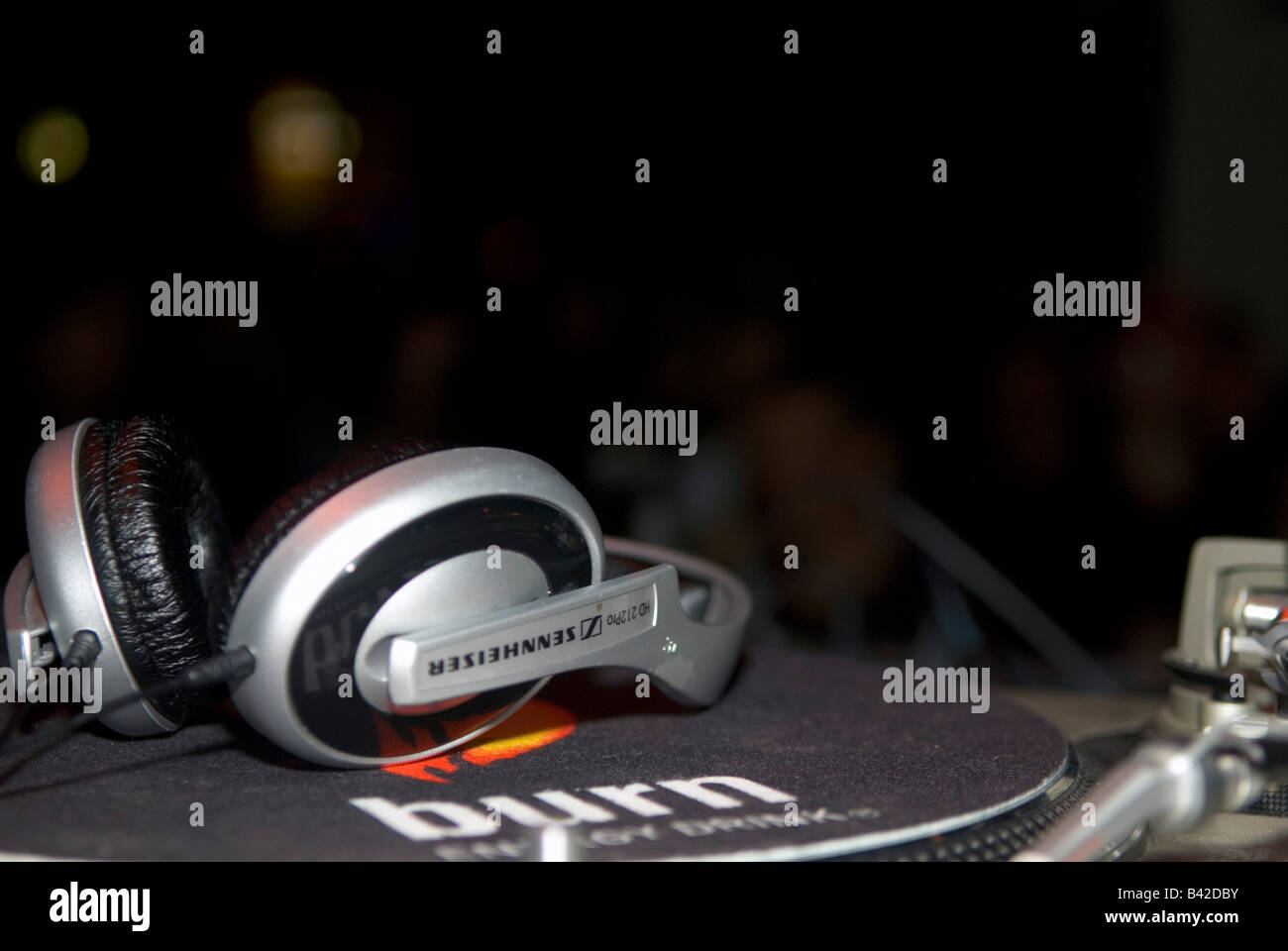 detail of headphones lying on a djs record deck with dancing crowd ...