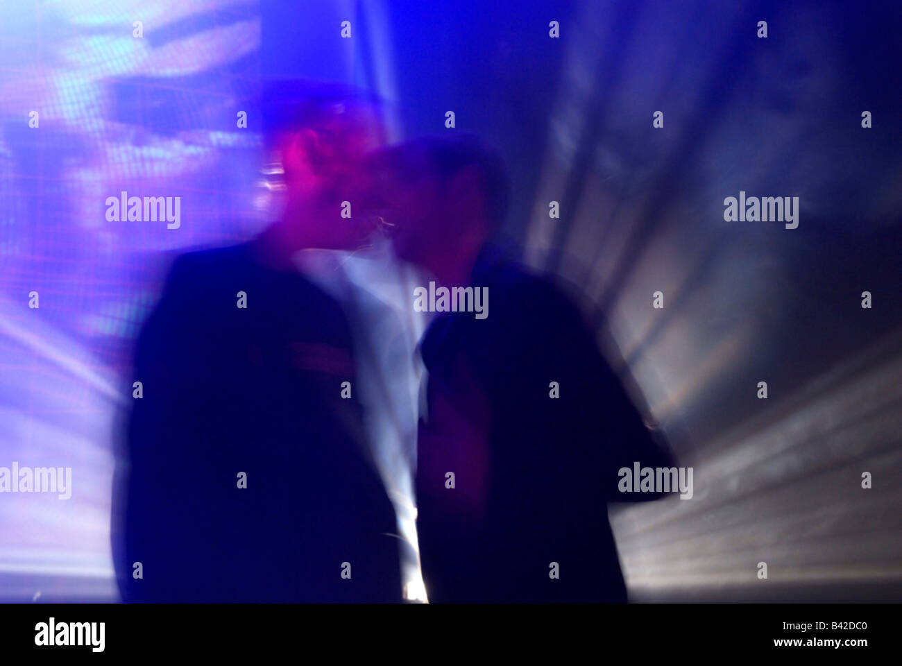 blurred shot of two men engaging in conversation at club with strobe ...