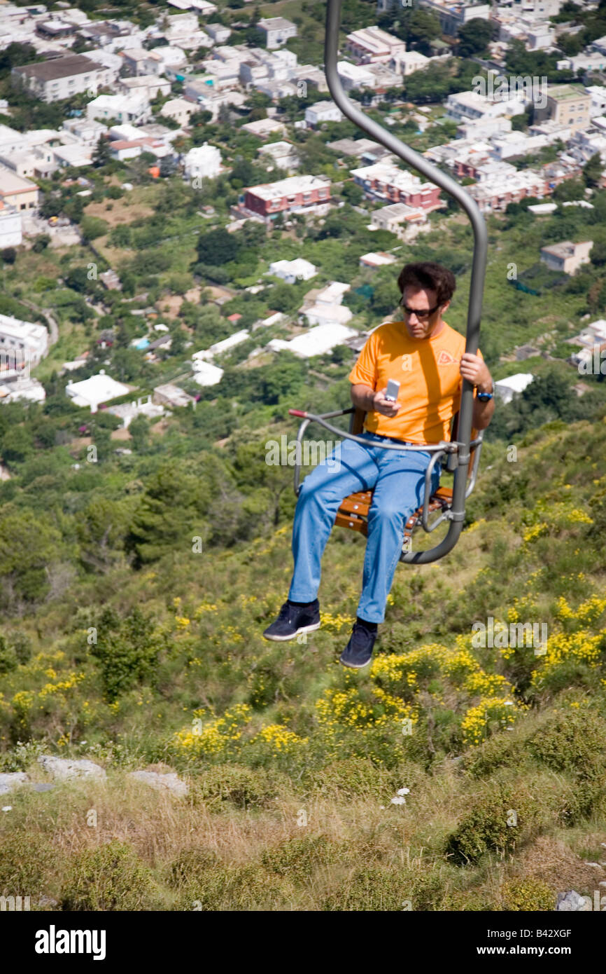 Man on chair lift looking at cell phone messages overlooking Capri, an ...