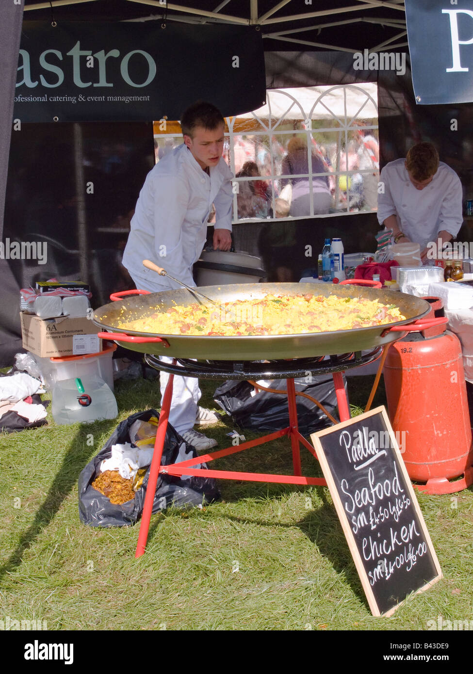 A young male chef cooking Paella in a large skillet outdoors at a ...