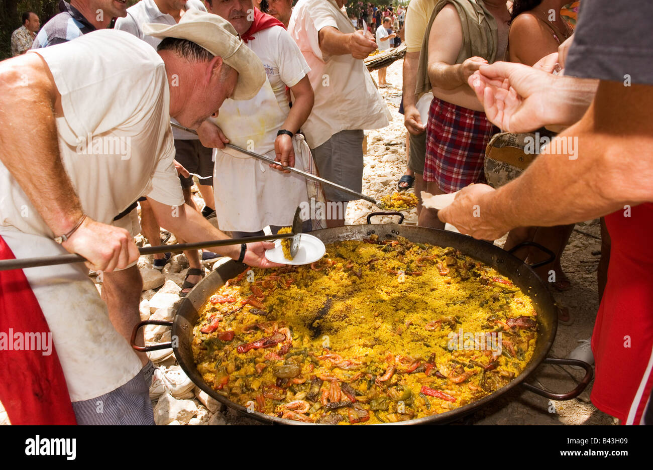 portions of a giant Paella are being dished out to hungry eaters in ...