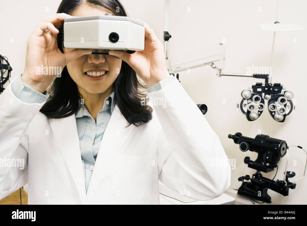 Asian female optometrist looking through equipment Stock Photo - Alamy