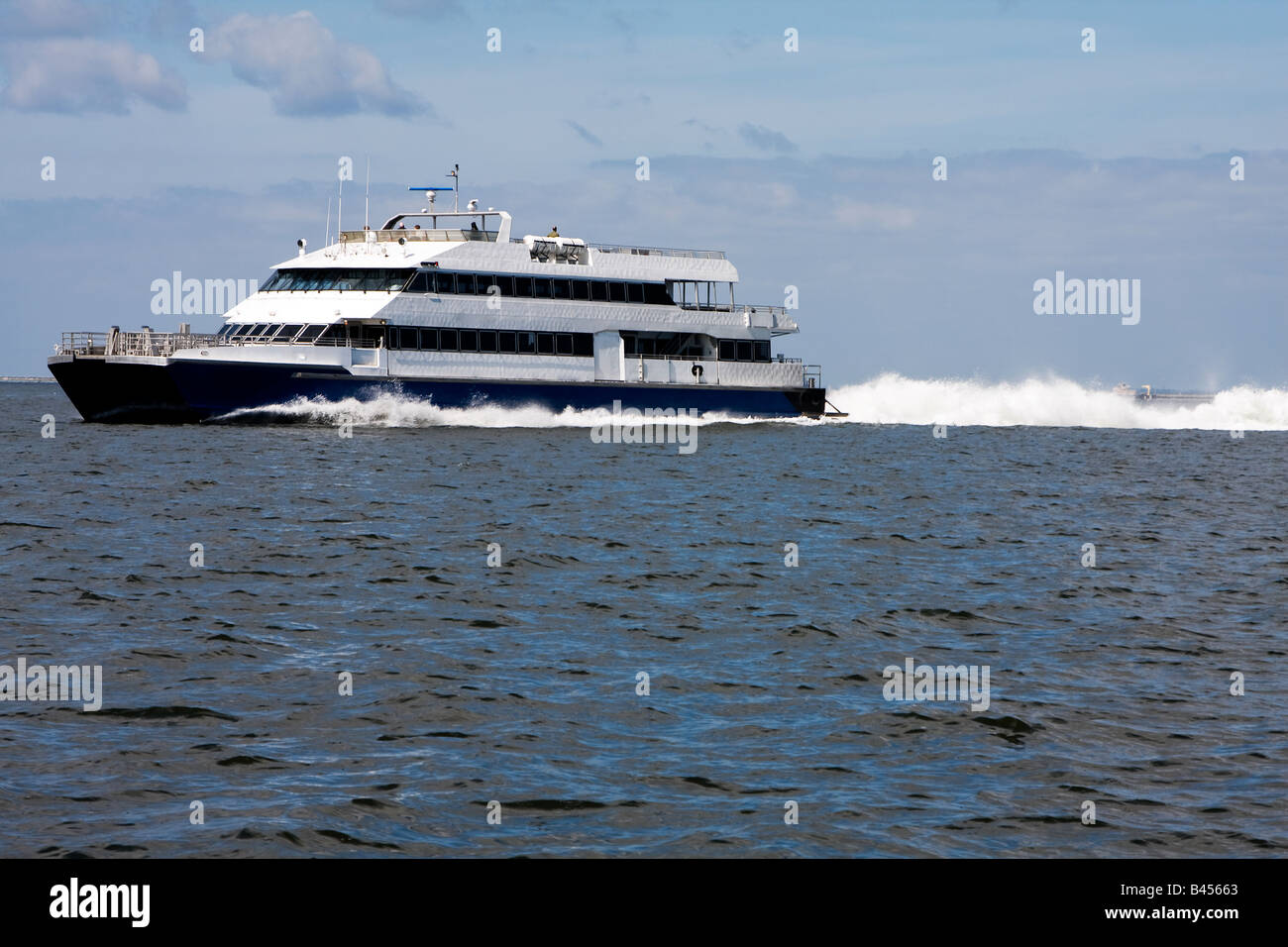 Blue with white catamaran ferry for commuters moving fast on open water ...