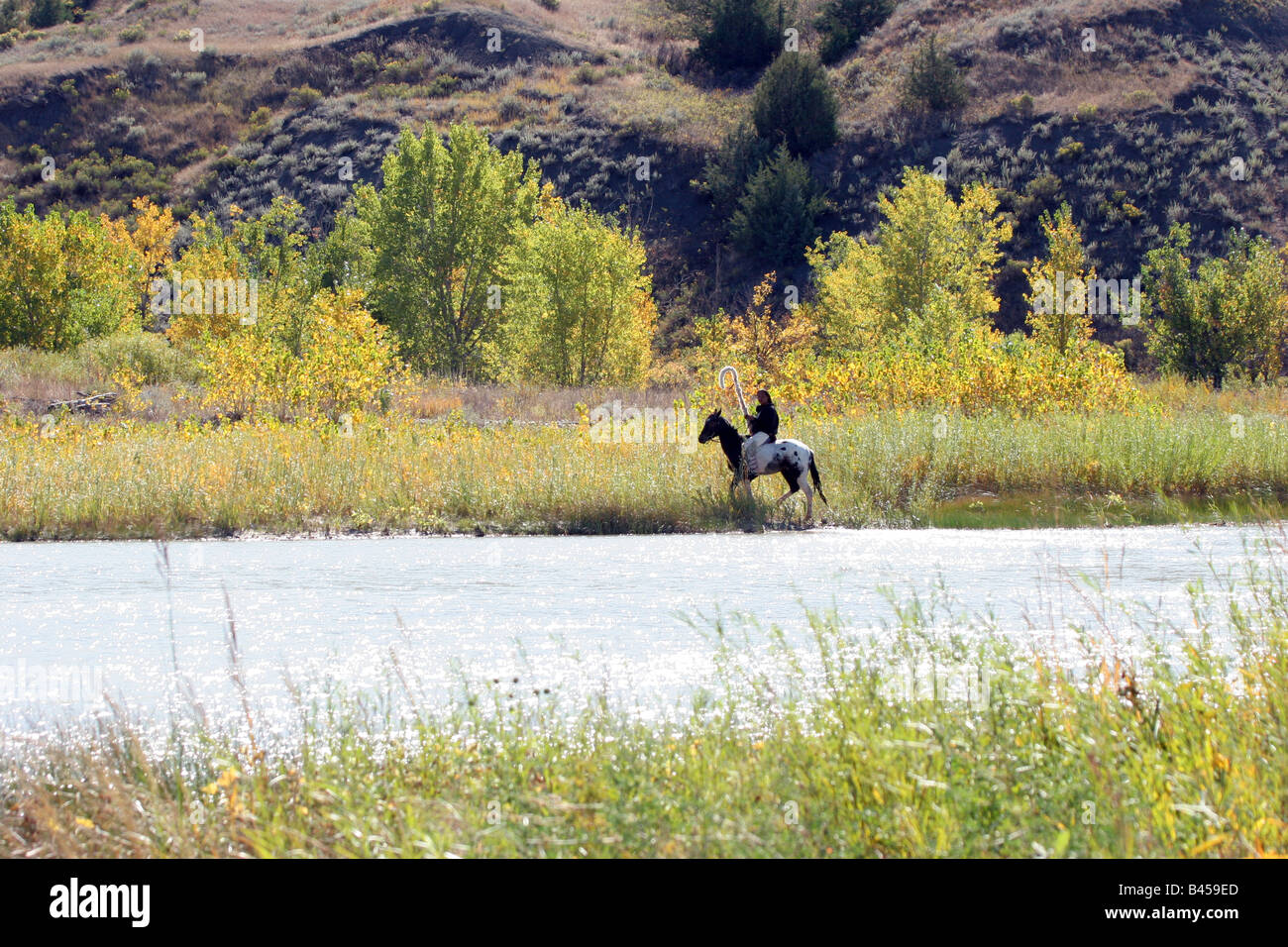 A Native American Sioux Indian on horseback riding across a river on ...