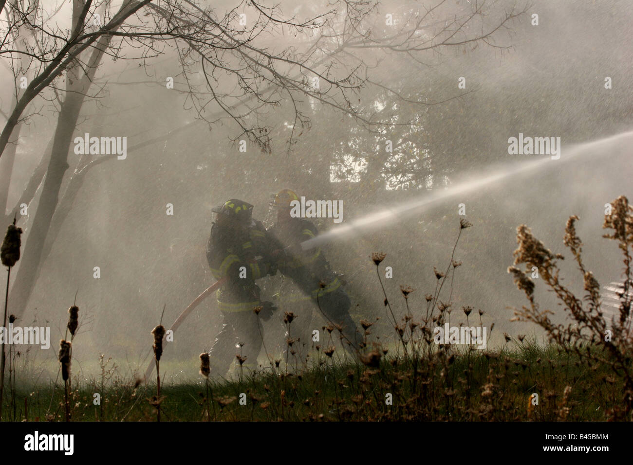 Two firefighters holding a hose while getting sprayed on from an aerial ...
