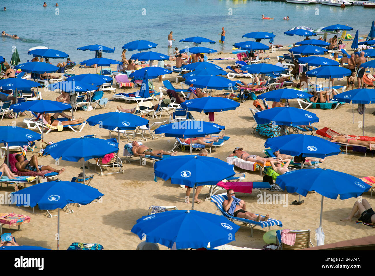 VIEW OF FIG TREE BAY, PROTARAS, IN CYPRUS WITH MANY BLUE UMBRELLAS AND ...