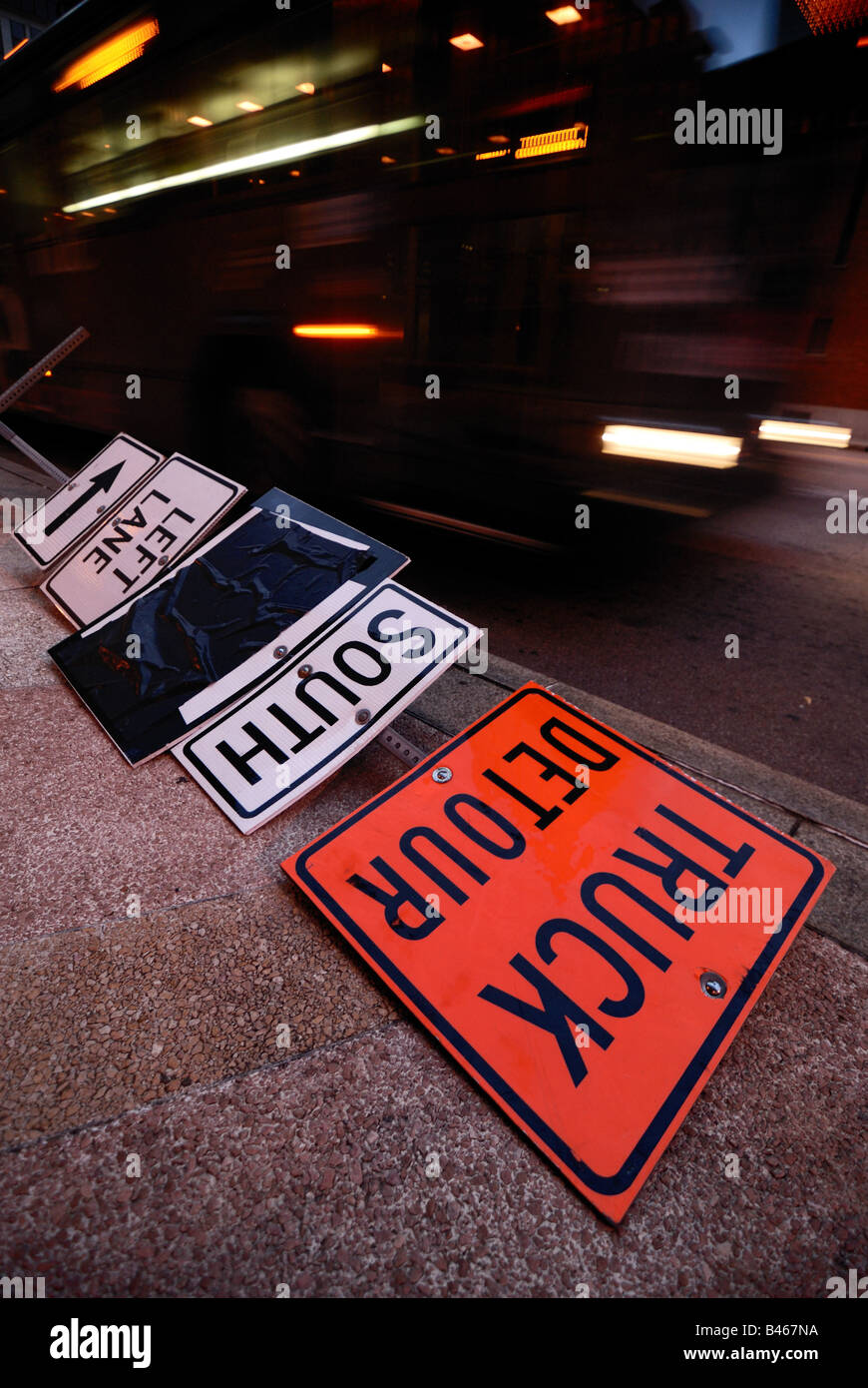 A detour sign that has been knocked over is lying on the sidewalk as a ...