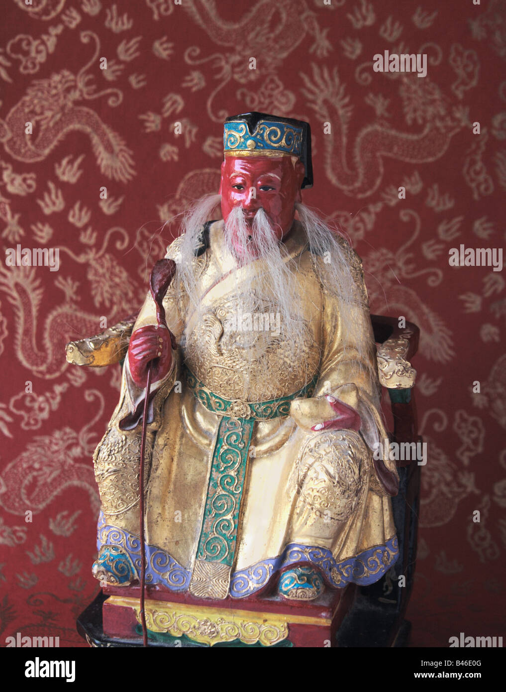 a colorful Chinese god in a decorative gold gown against a red dragon ...