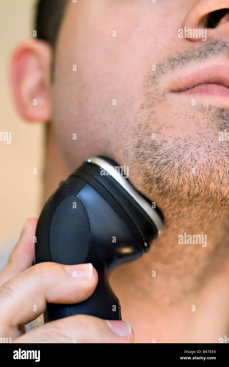 A closeup of a young man shaving his beard off with an electric shaver ...