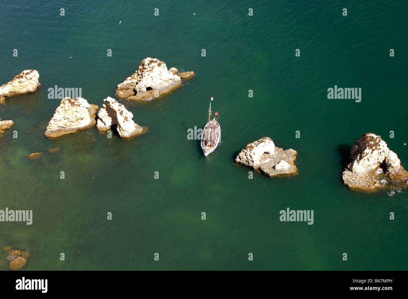 A small tourist boat navigates between rocks off the coast line near ...