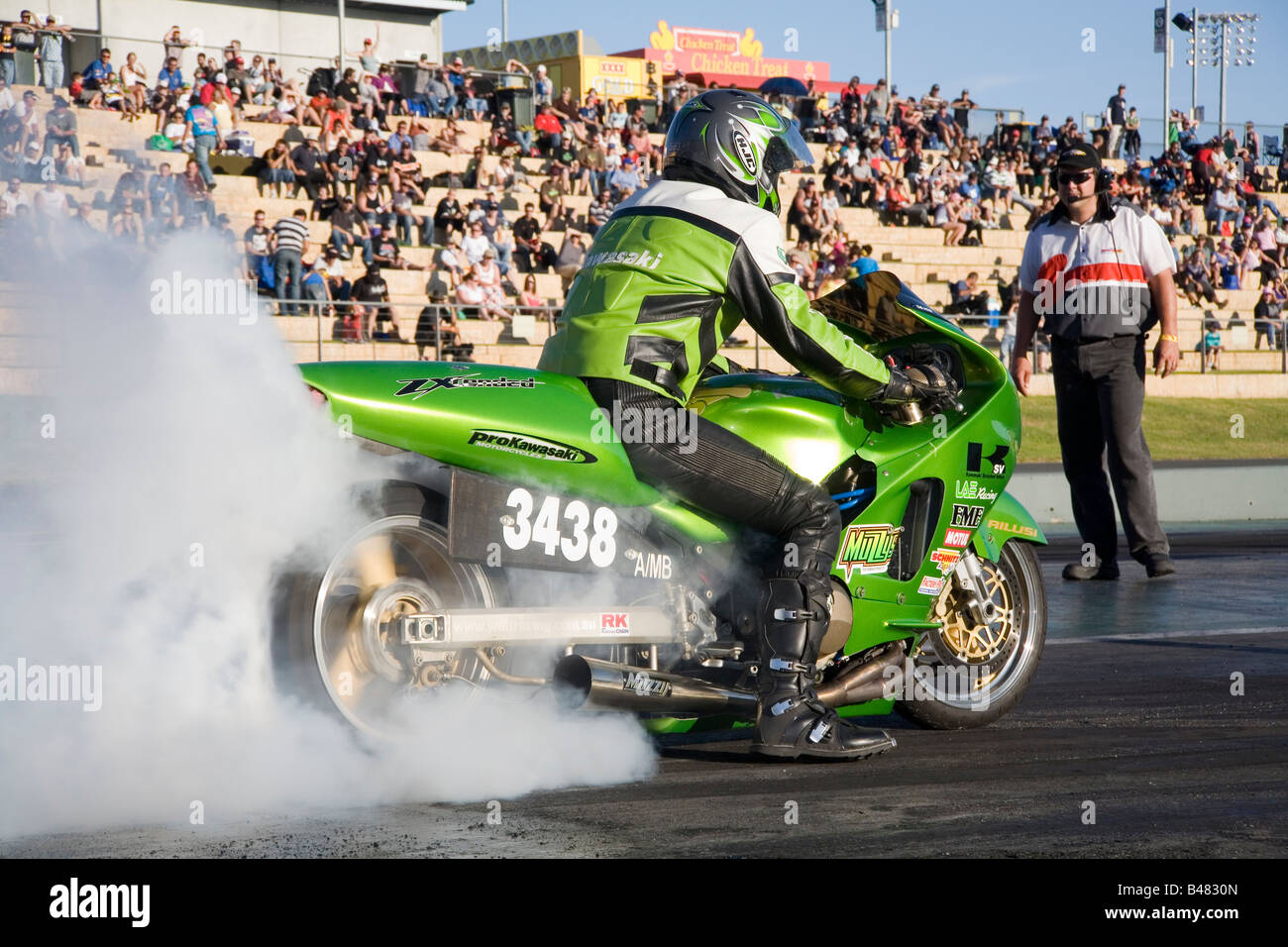 A Kawasaki drag racing motorcycle performs a burnout to warm the rear ...