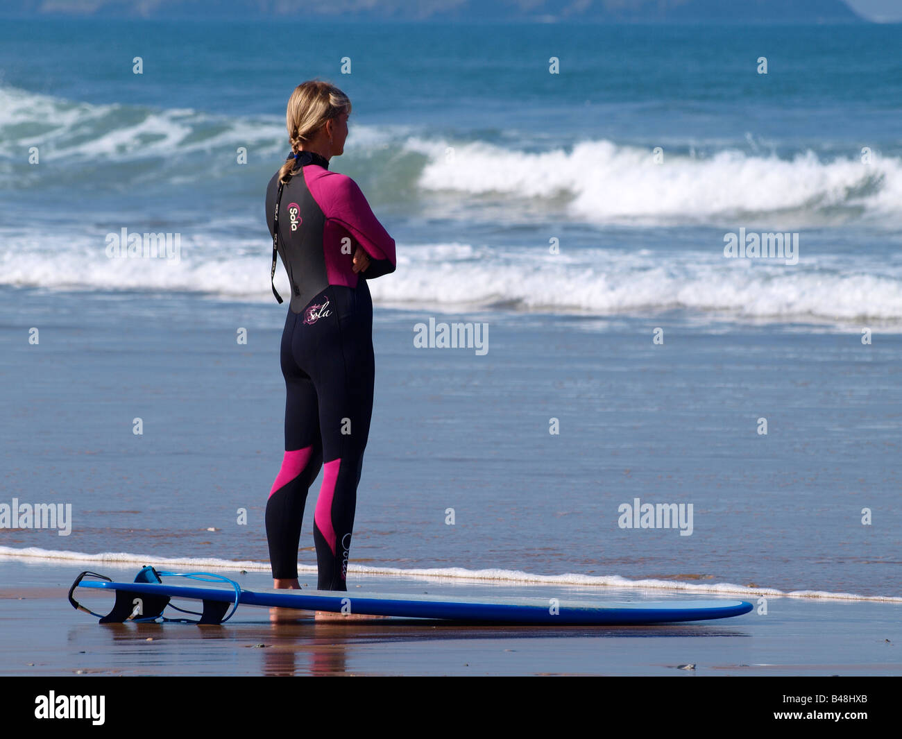 Blonde female surfer standing at the edge of the water looking at the ...