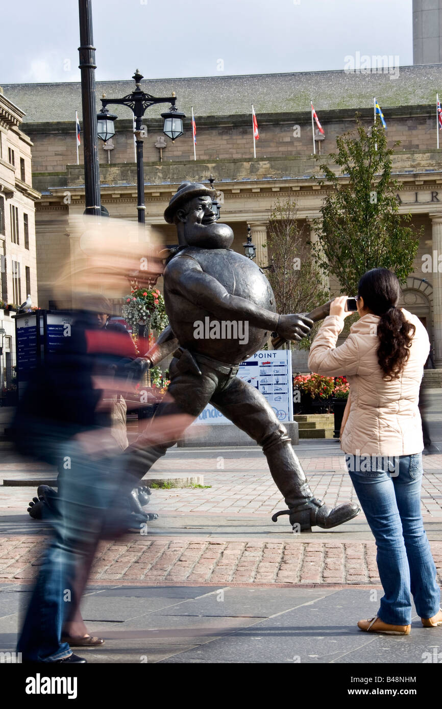 Tourist taking a photograph of Desperate Dan statue in the city centre ...