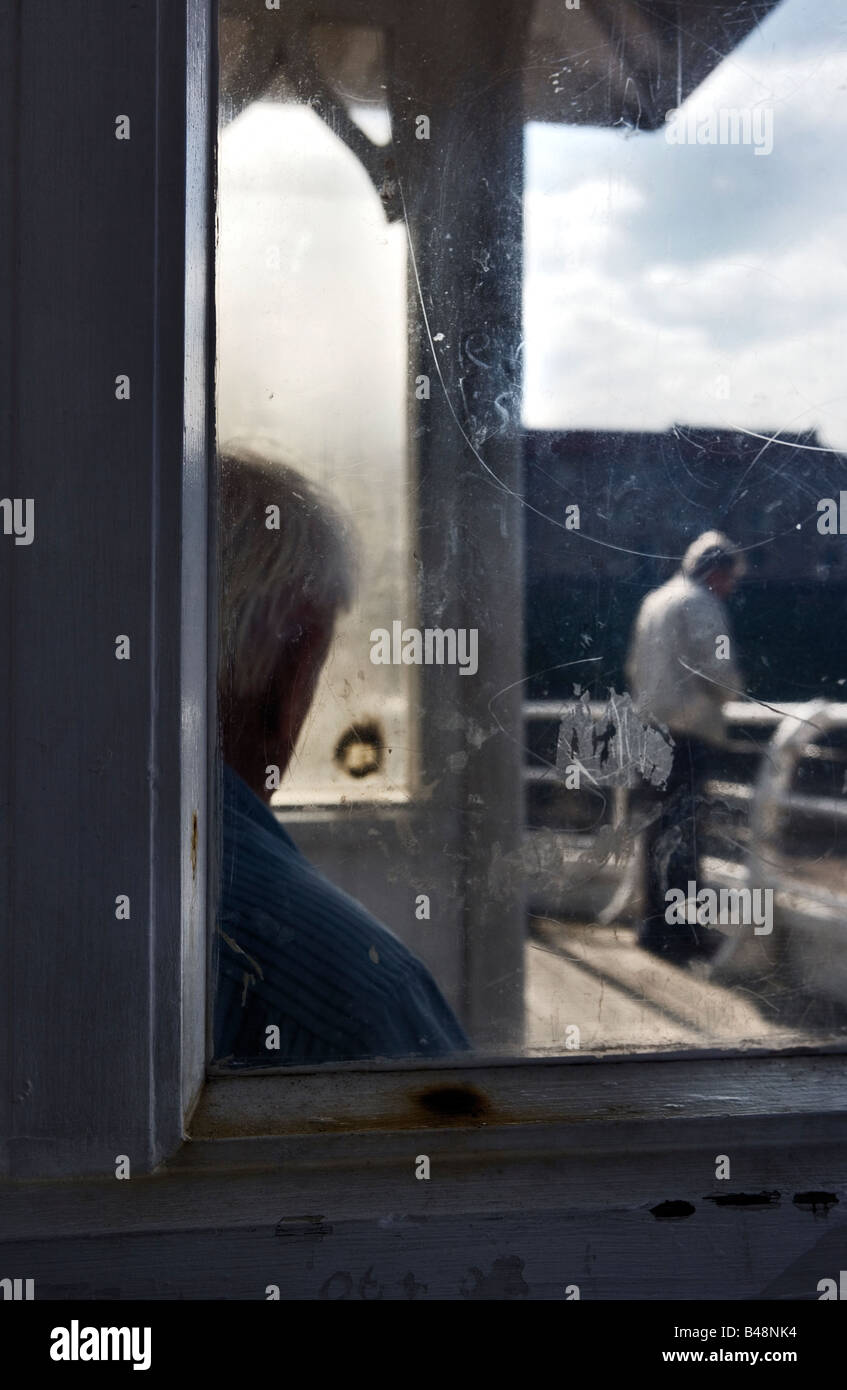 Two elderly men on a seaside pier; glass in window of the shelter is ...
