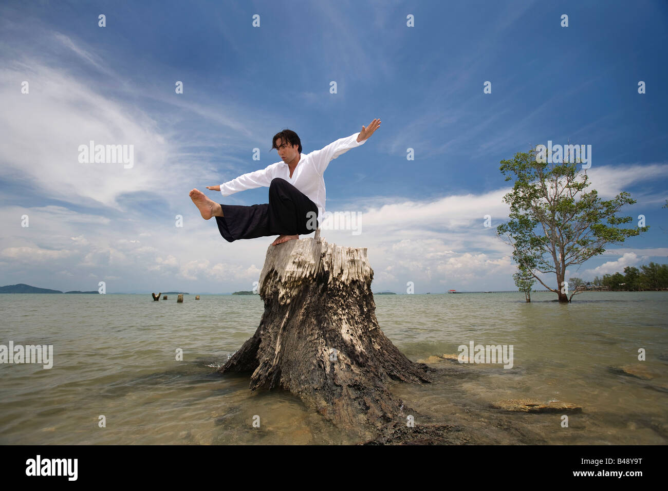 A man balancing on a tree stump on a beach in Koh Lanta, Thailand Stock ...