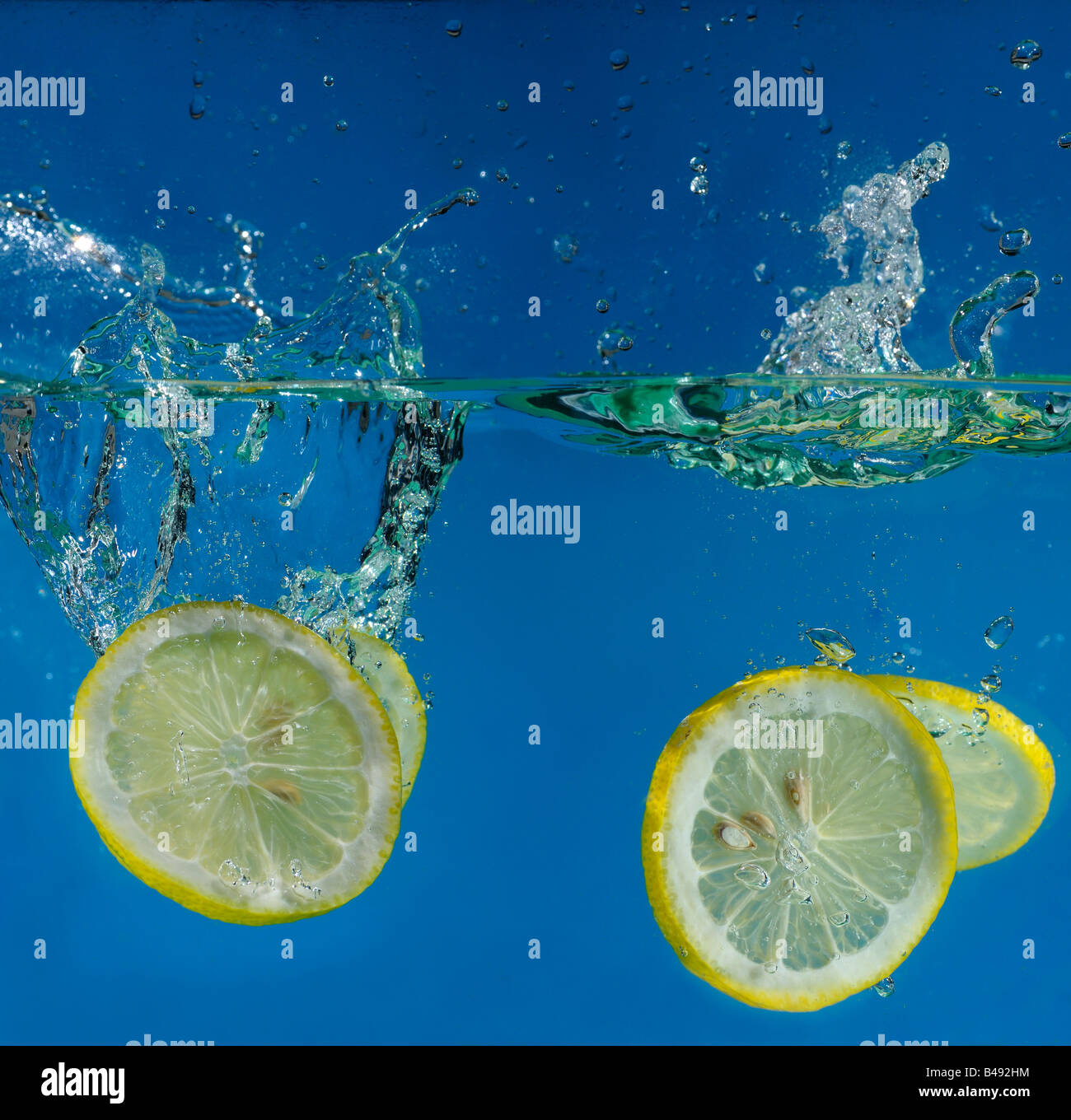 Two pairs of fresh lemon slices splashing into a water tank with a blue ...