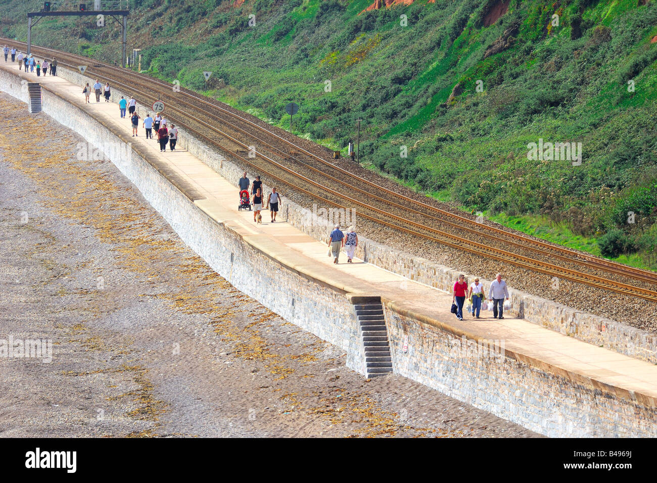 Tourists walking along the seafront promenade beside the railway track ...