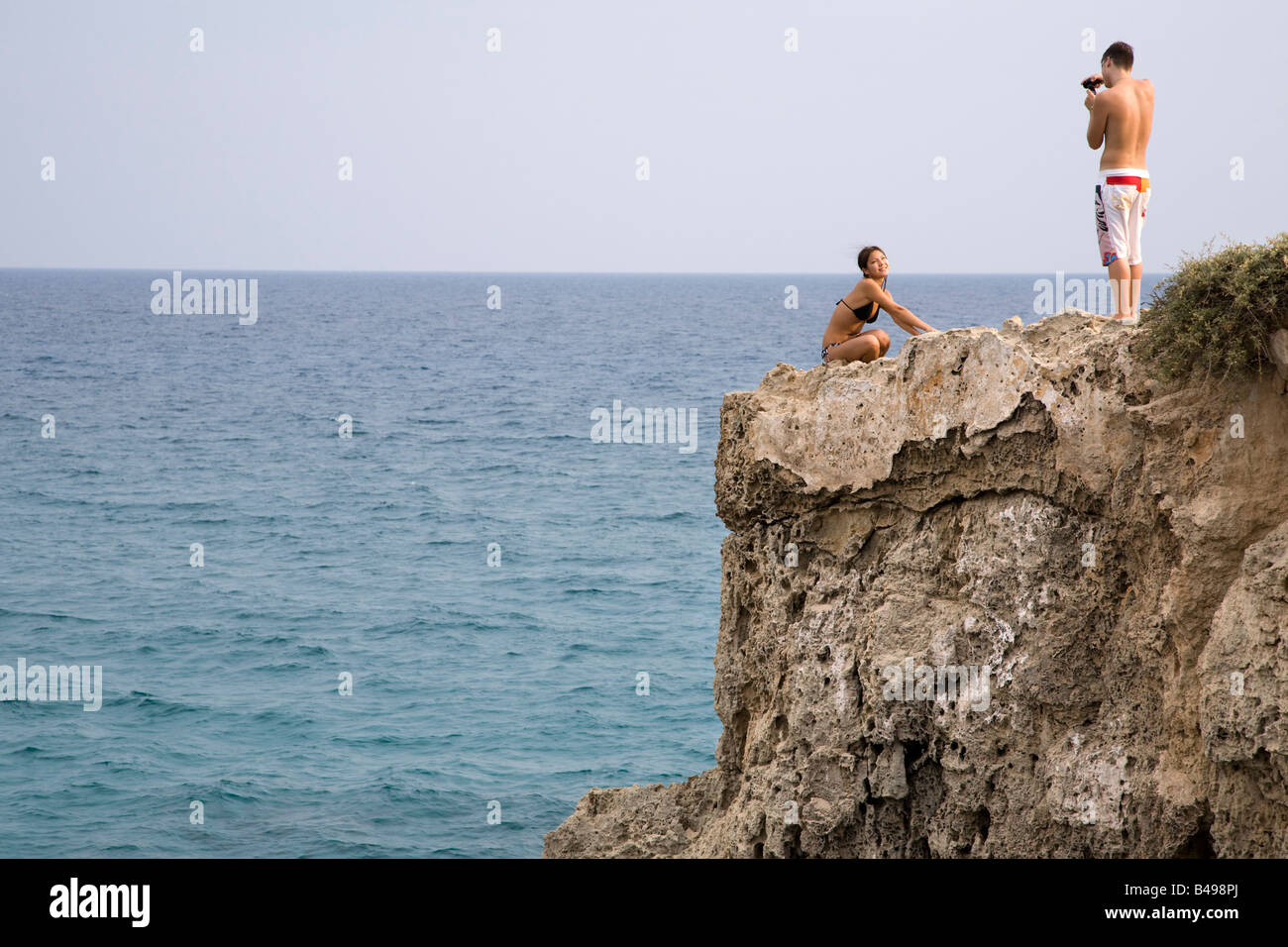 A MAN TAKES A PHOTO OF HIS FRIEND ON THE EDGE OF A ROCK OVERLOOKING THE ...