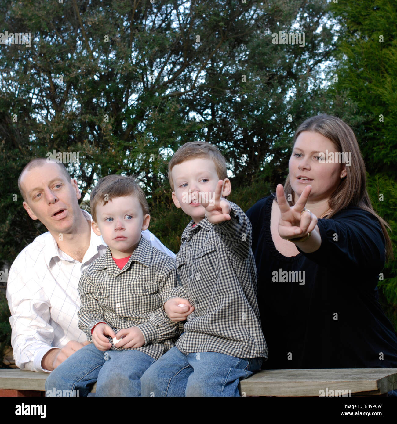 A young family with twin boys practicing making the hand sign for peace ...