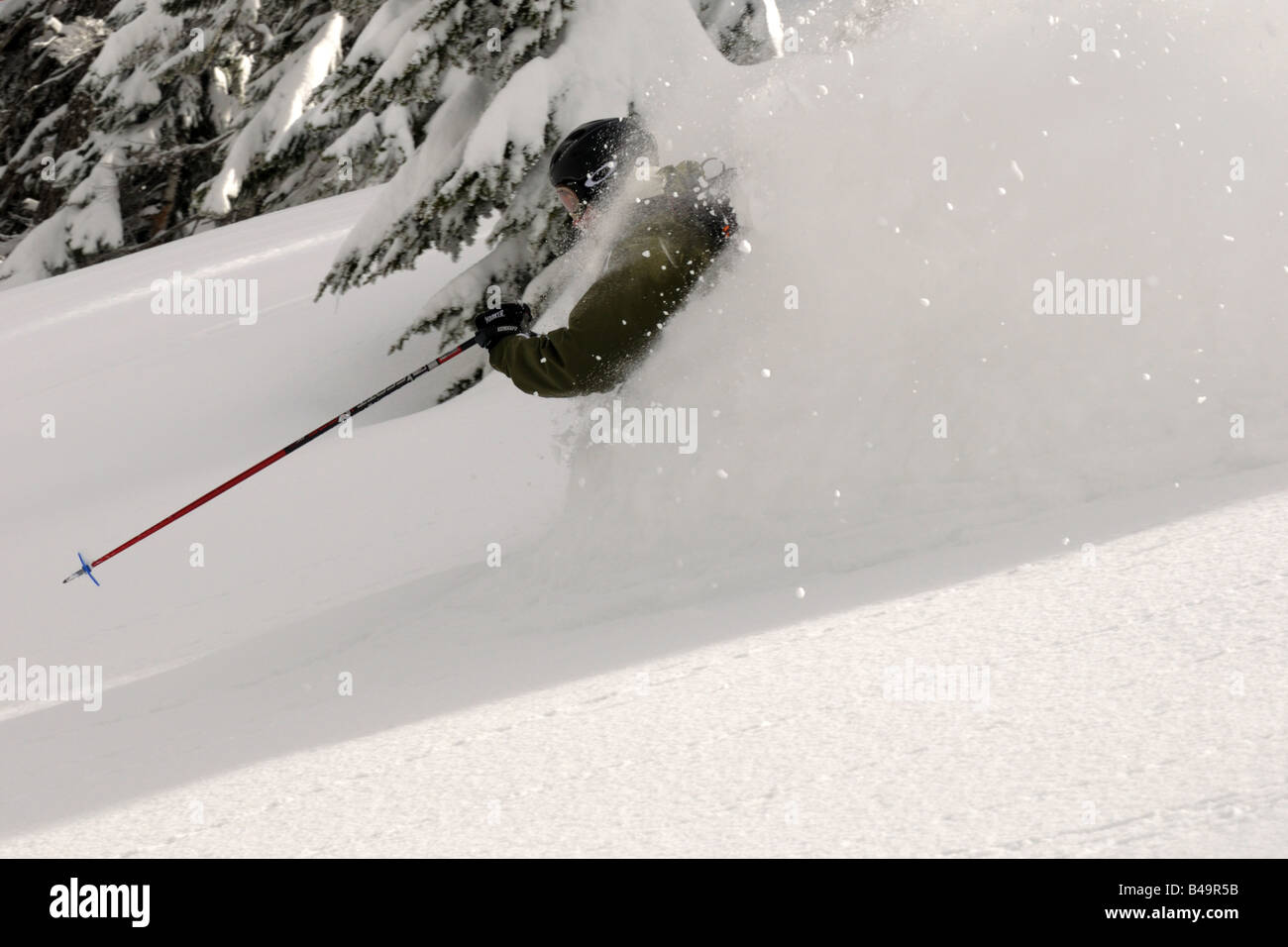 A skier in deep powder snow with a large spray of snow over his ...