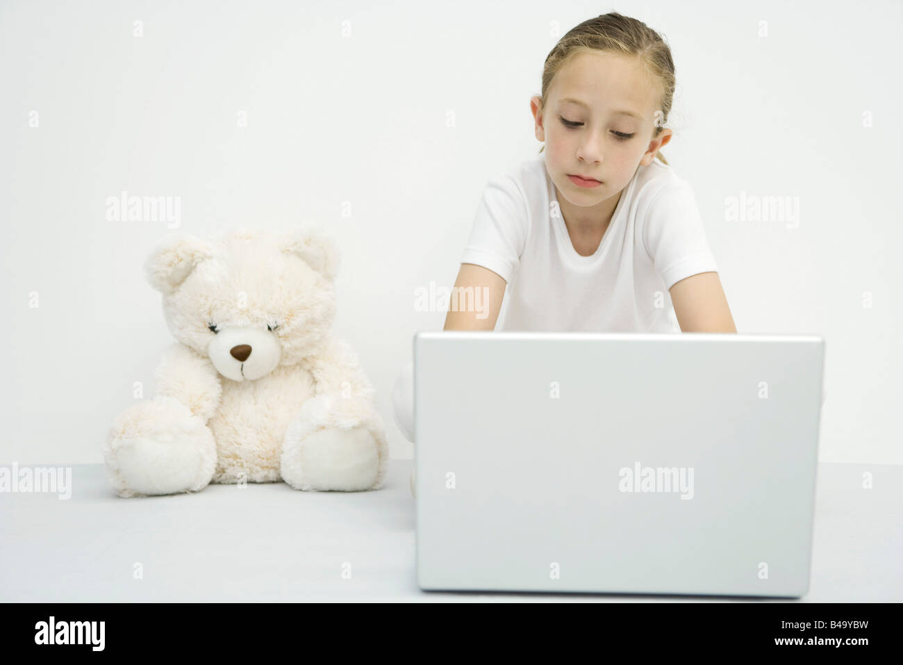 Girl sitting beside teddy bear, using laptop computer Stock Photo - Alamy