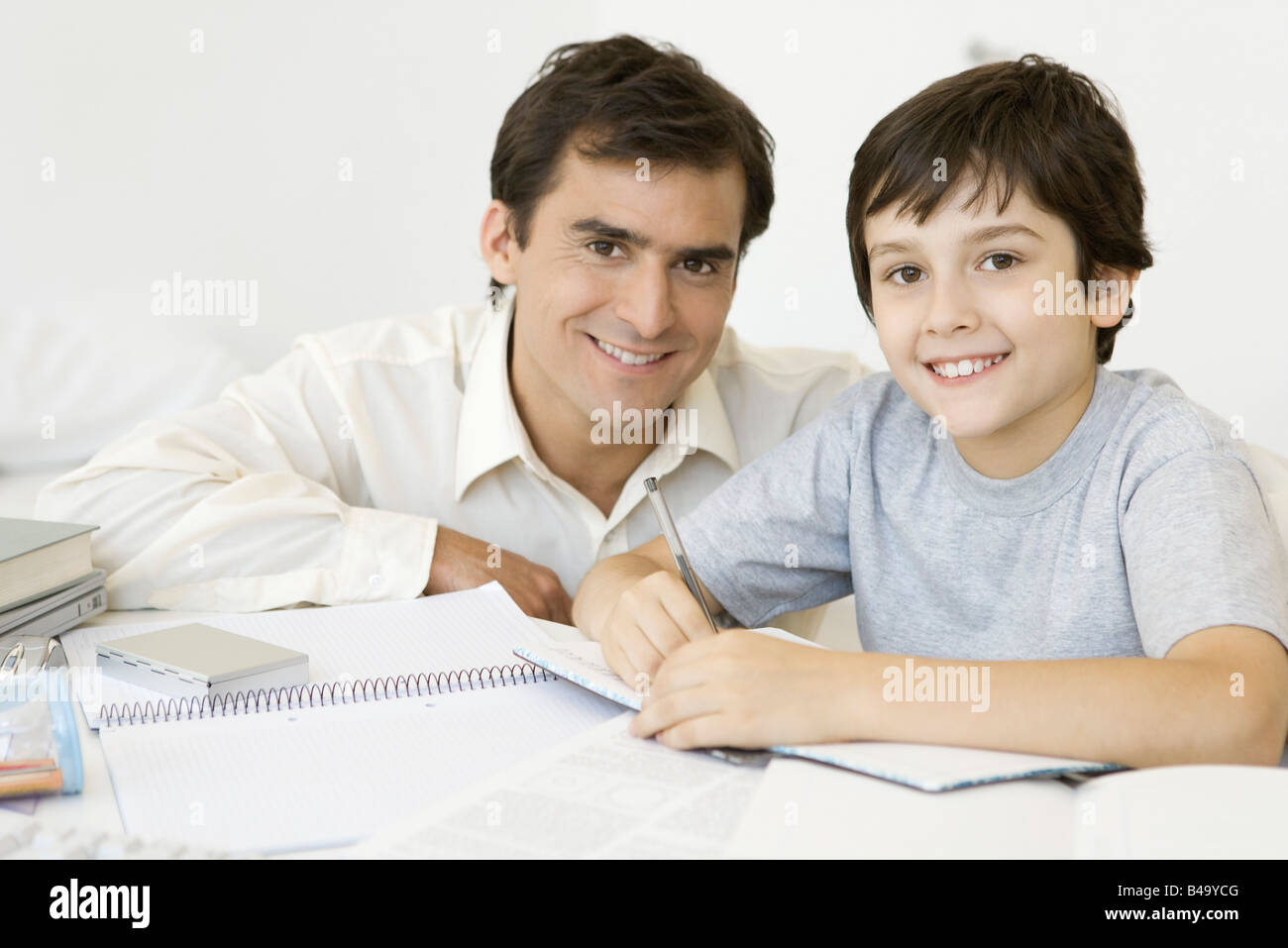 Boy doing homework with father, both smiling at camera Stock Photo - Alamy
