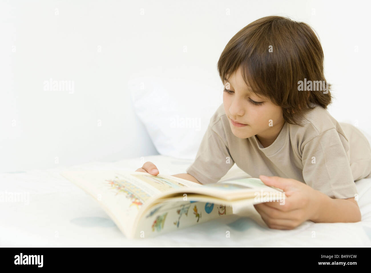 Boy lying on stomach, reading book Stock Photo - Alamy