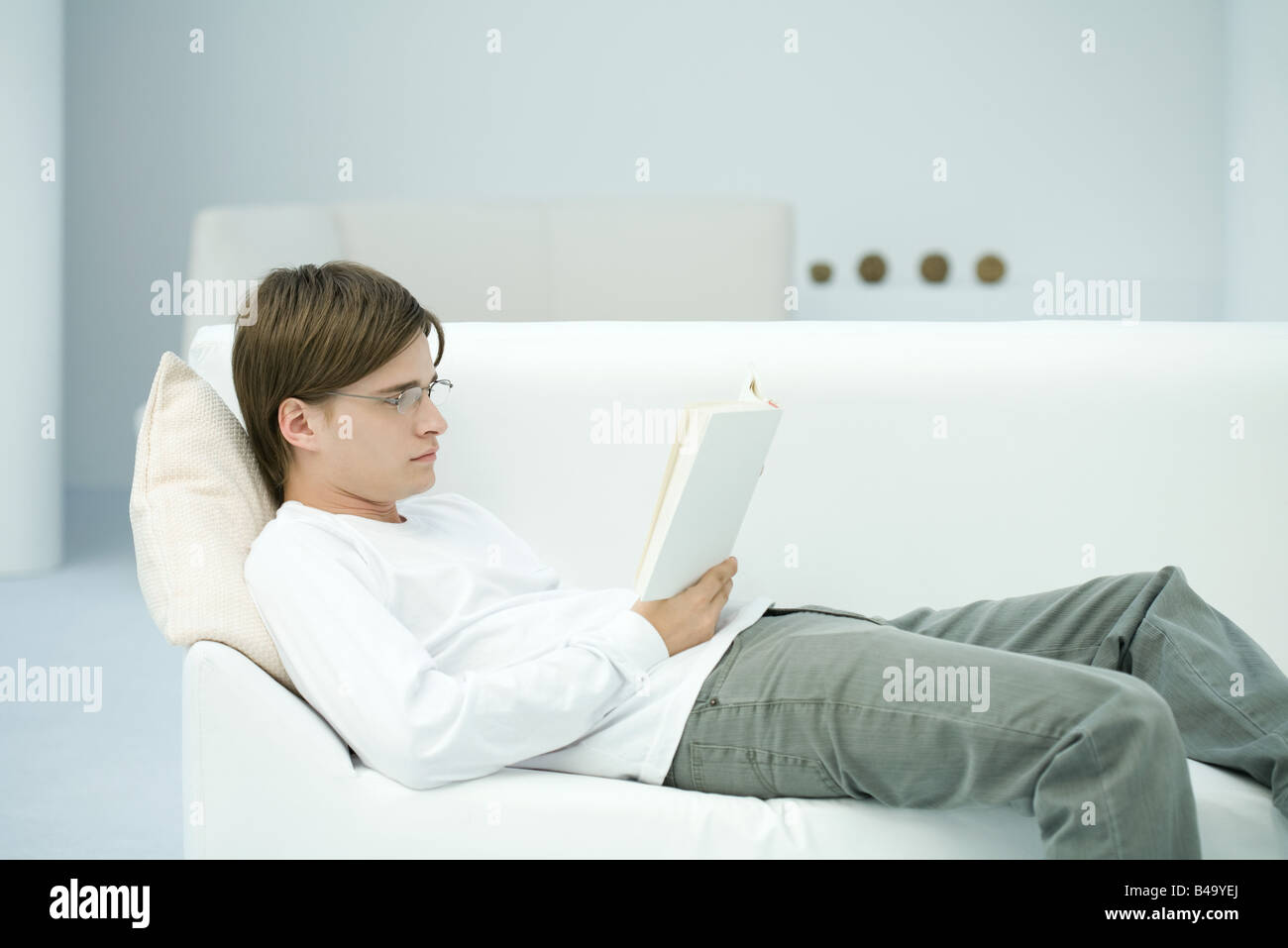 Young man reclining on sofa, reading book, side view Stock Photo - Alamy