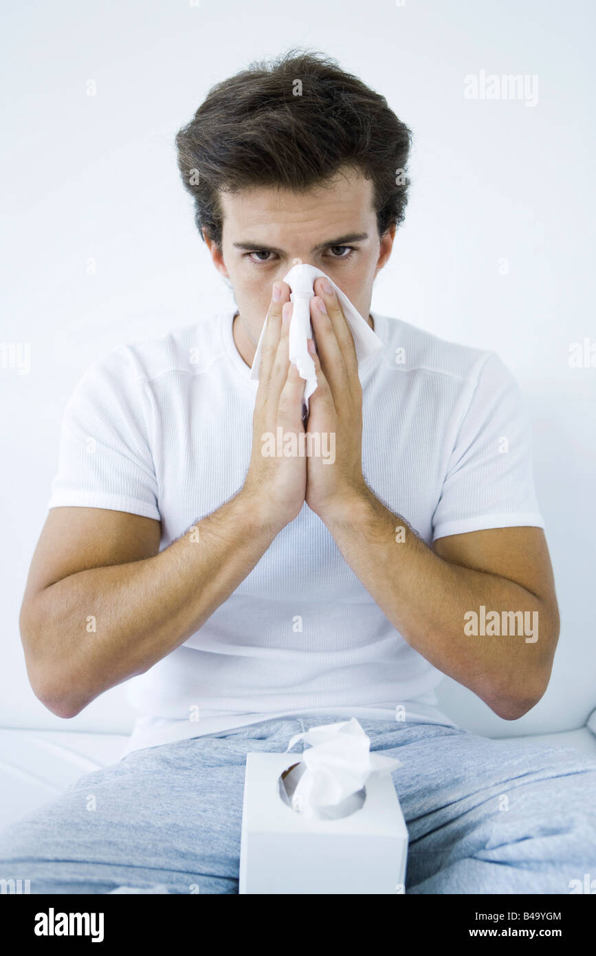 Man blowing his nose with a tissue, looking at camera Stock Photo - Alamy