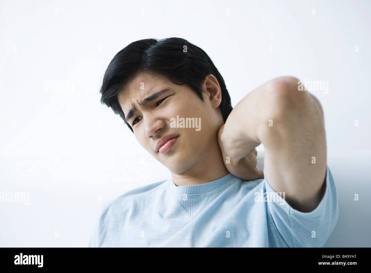 Young man holding neck, furrowing brow Stock Photo - Alamy