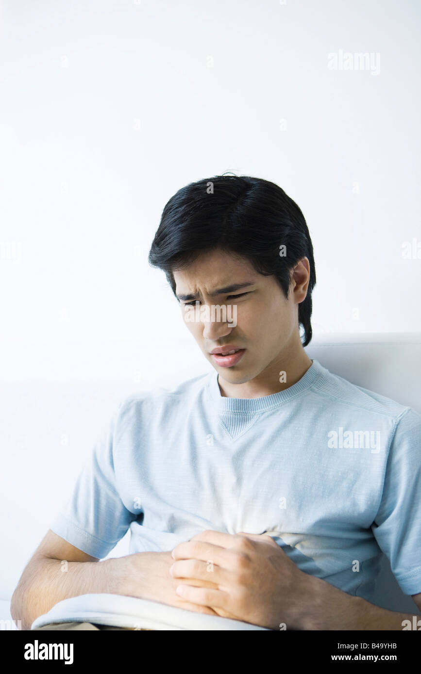 Young man holding his stomach and furrowing his brow Stock Photo - Alamy