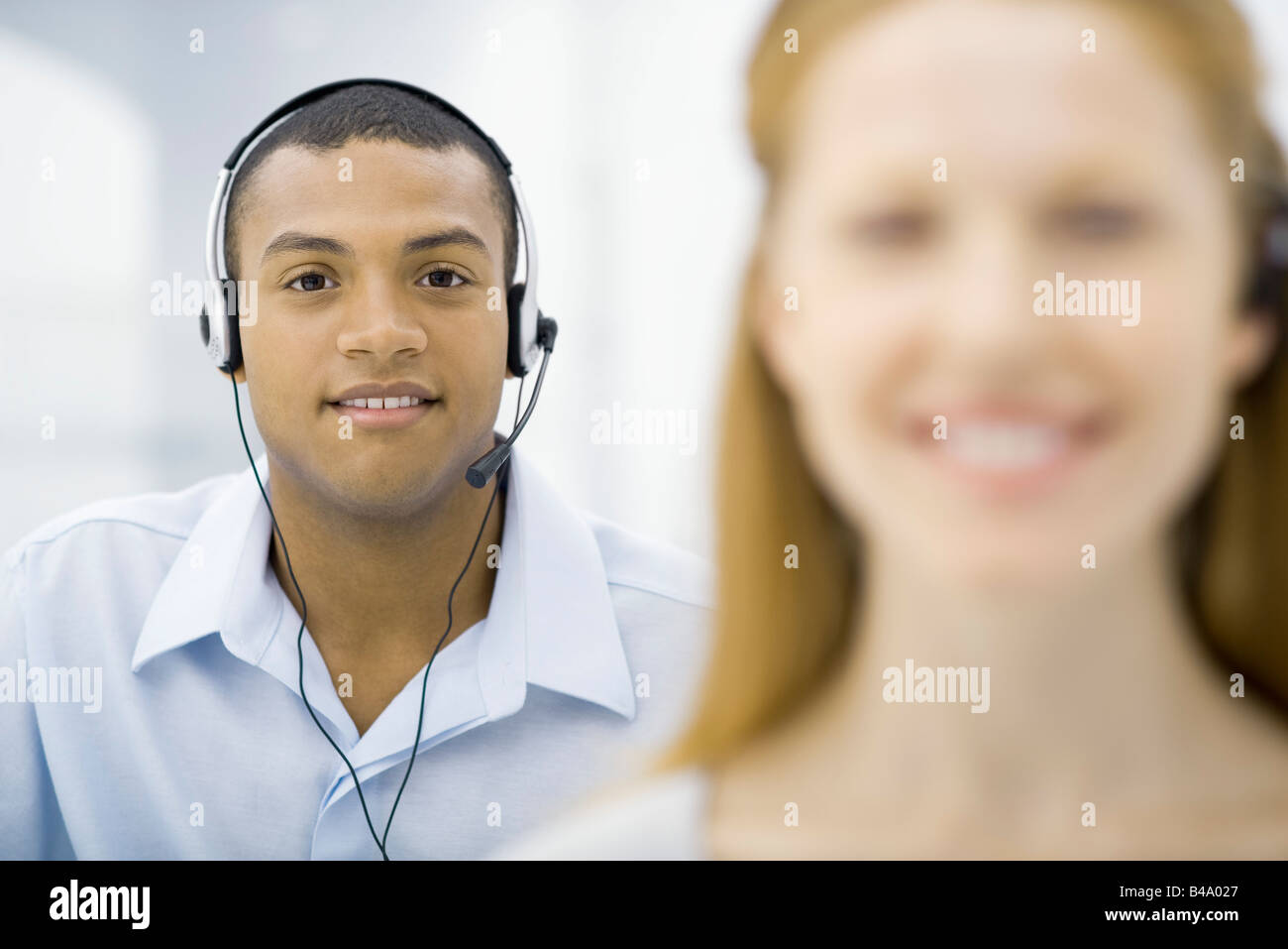 Professional man wearing headset smiling at camera, female colleague in ...