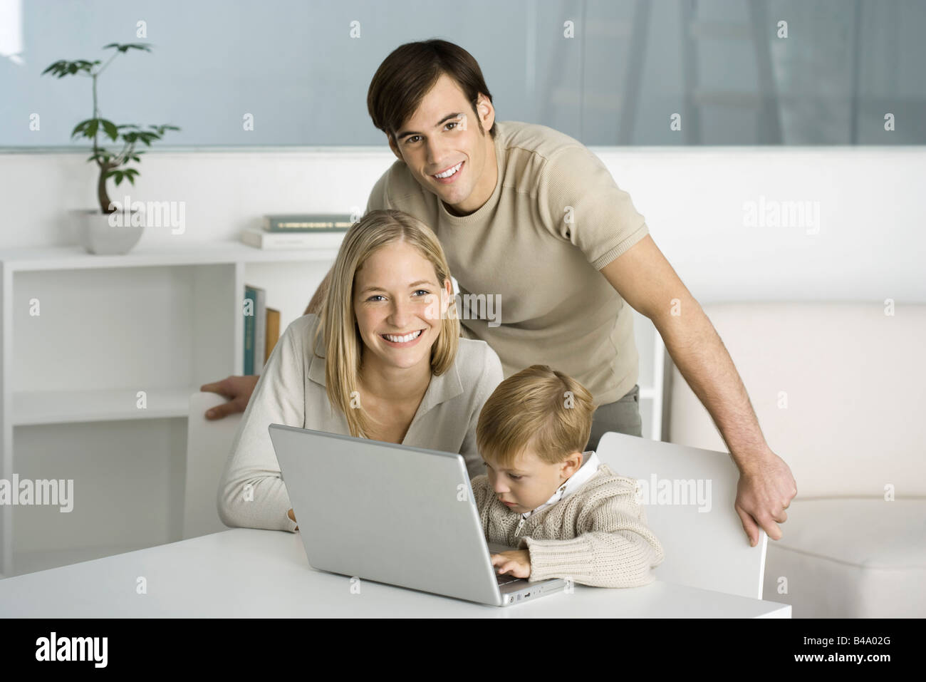 Family gathered around laptop computer, little boy typing, parents ...