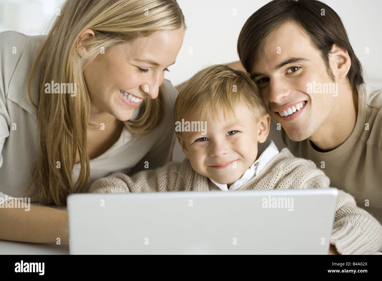 Family gathered around laptop computer, father and son smiling at ...