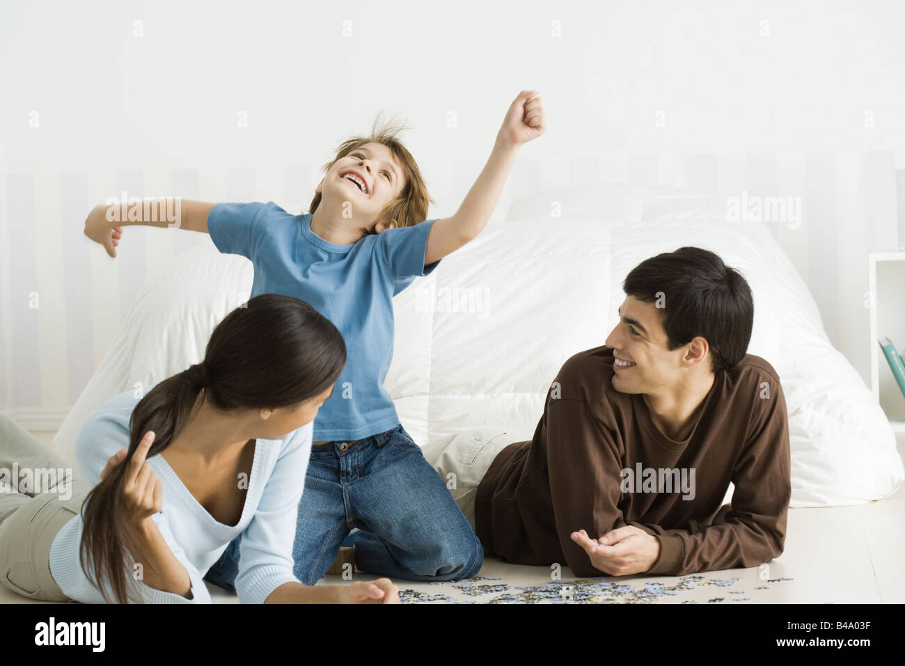 Family playing with jigsaw puzzle in bedroom, boy laughing, arms raised ...