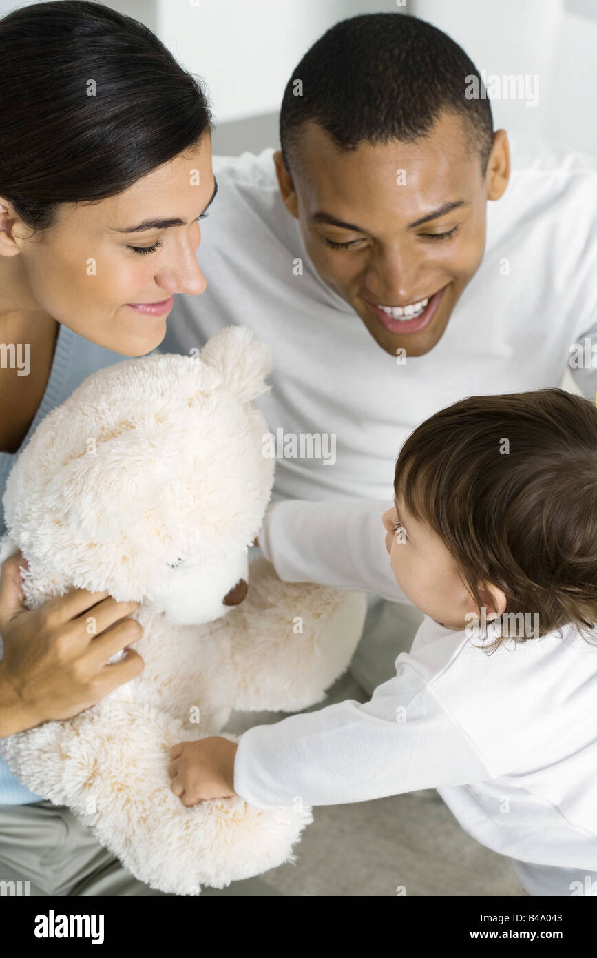 Parents giving toddler daughter a teddy bear, high angle view Stock ...