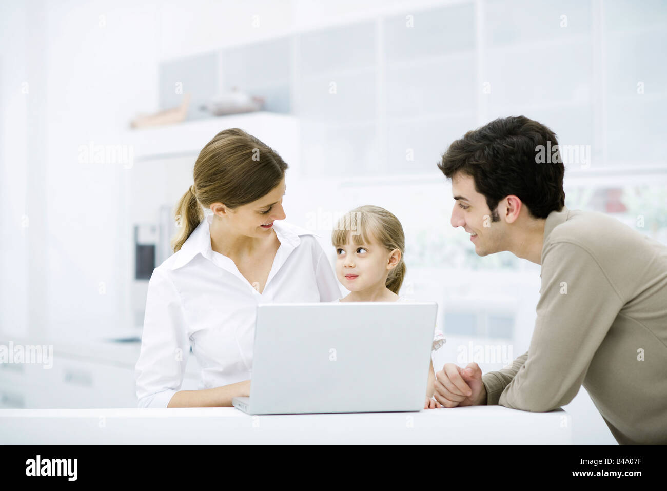 Family gathered around laptop computer, smiling, girl looking at mother ...