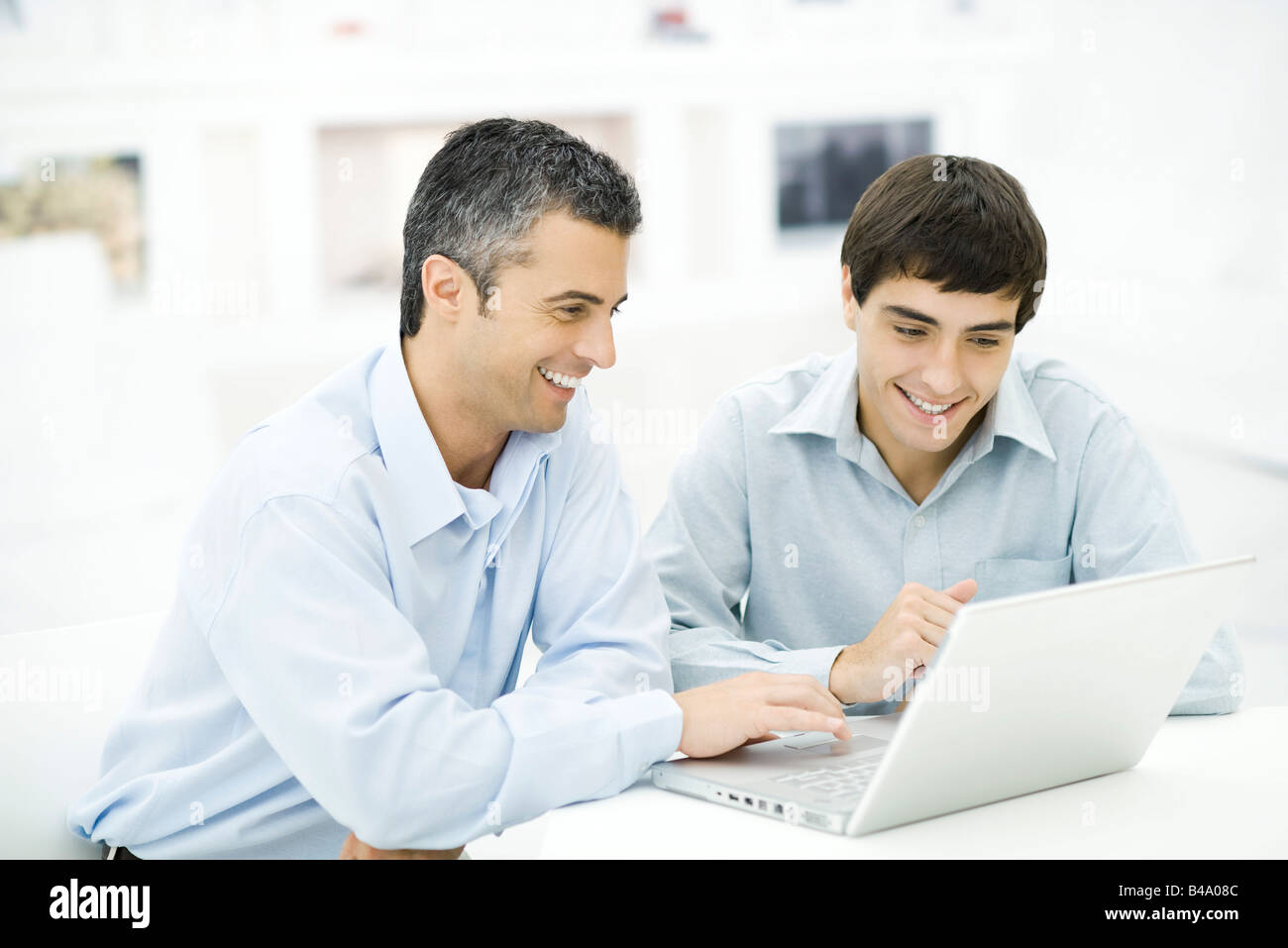 Father and adult son looking at laptop computer together, smiling Stock ...