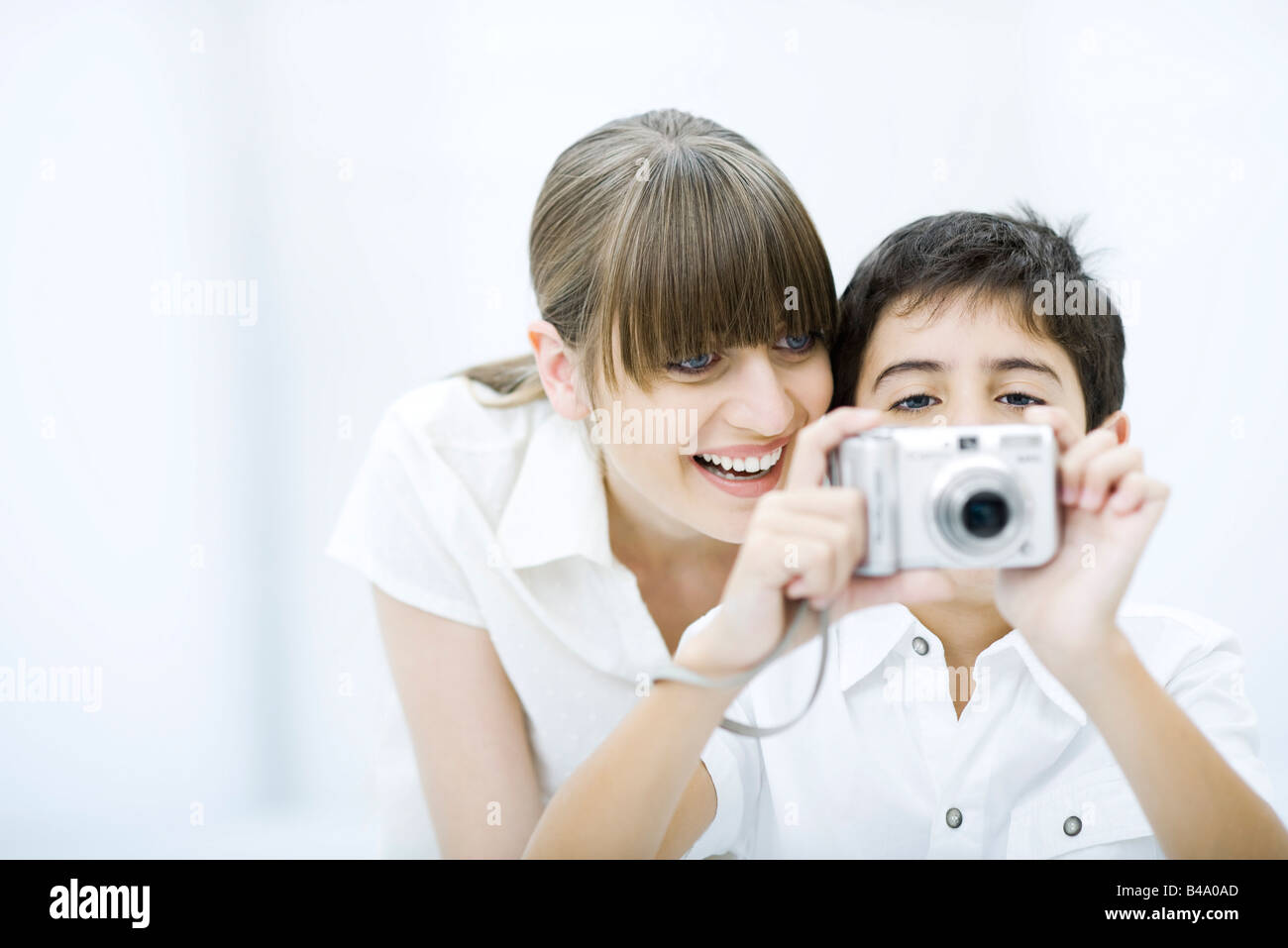 Boy taking picture with camera, mother leaning over his shoulder ...