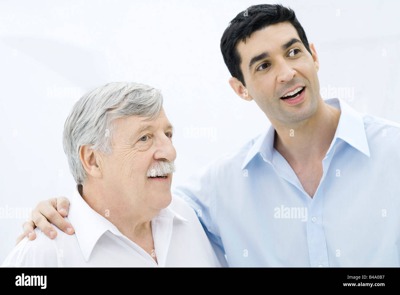 Father and adult son looking away, smiling, son's arm around father's ...
