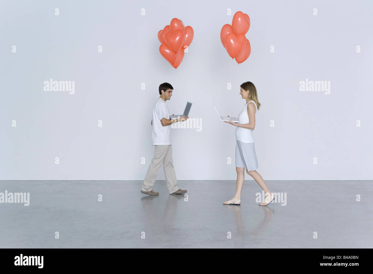 Young man and woman walking toward each other, both carrying laptop ...