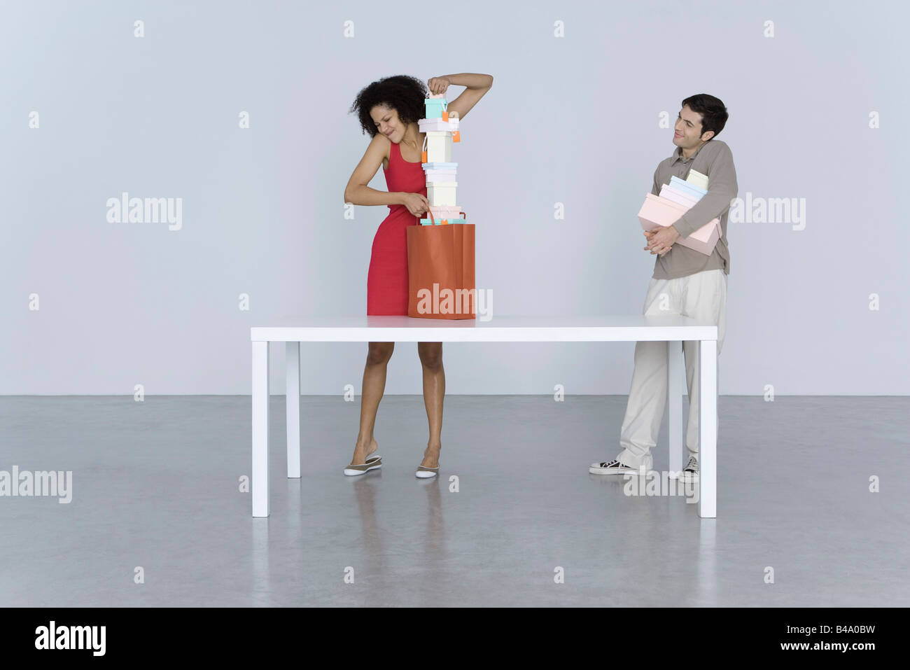 Woman shoving large stack of boxes into shopping bag, man standing ...