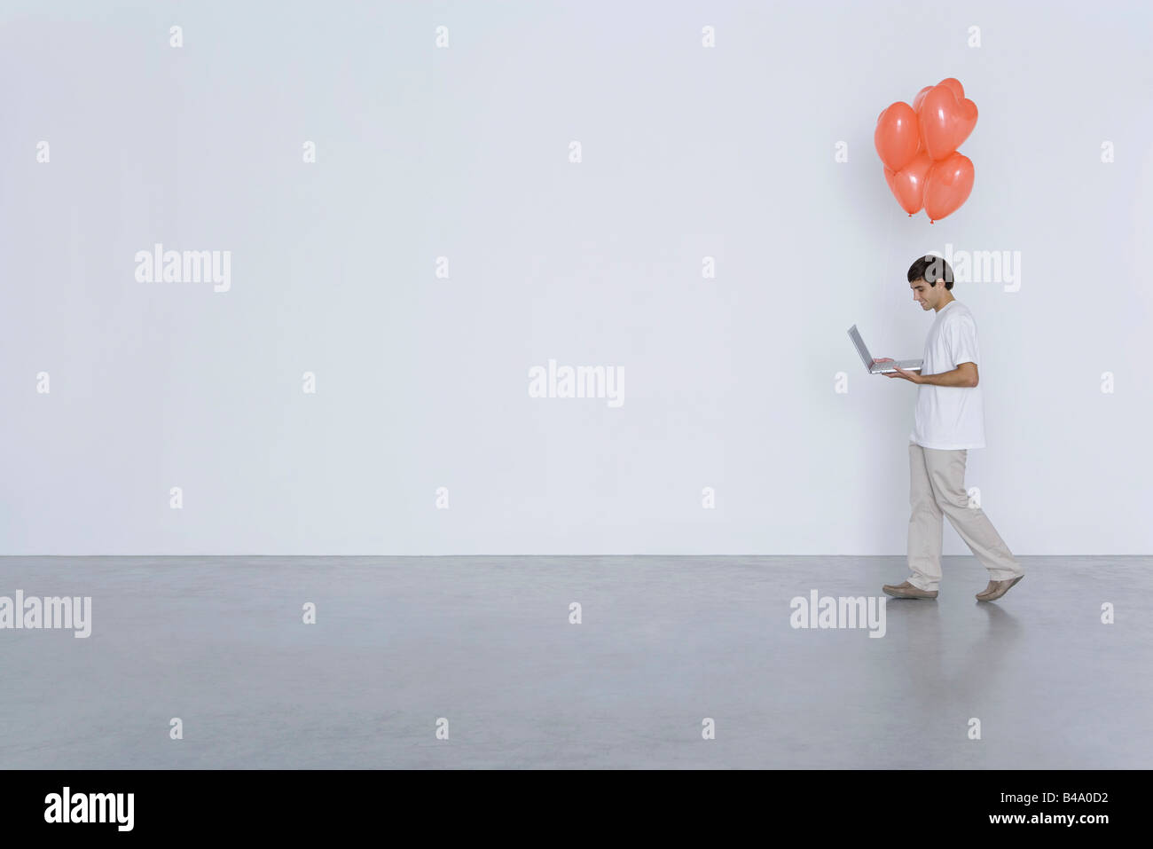 Man carrying laptop computer and heart balloons, side view Stock Photo ...
