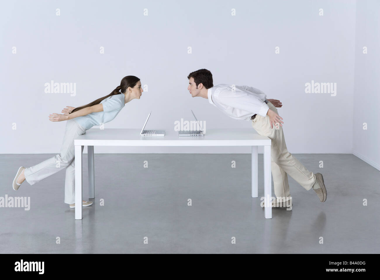 Man and woman at opposite ends of table, leaning towards each other ...