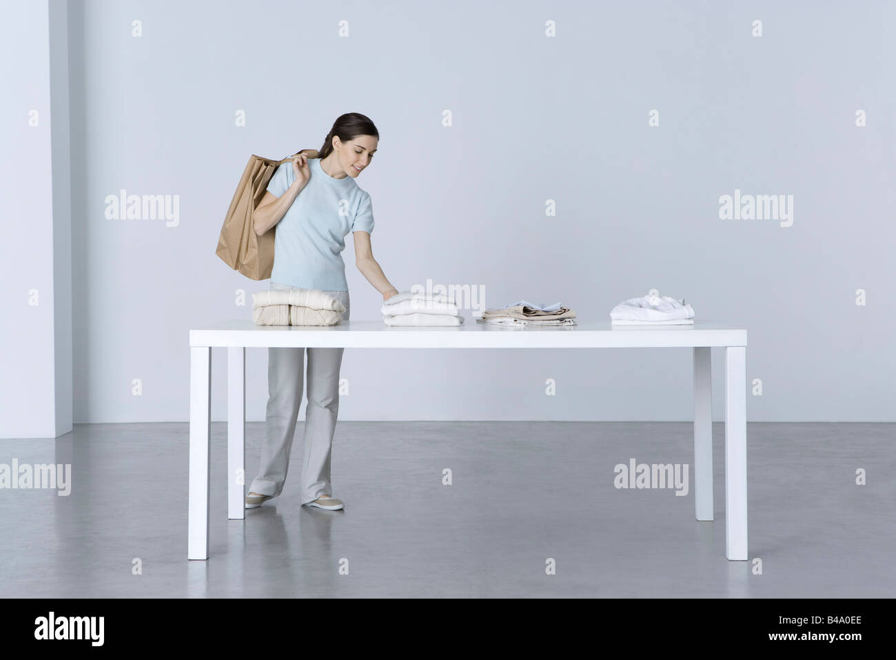 Woman looking at clothing folded on table, shopping bags slung over her ...