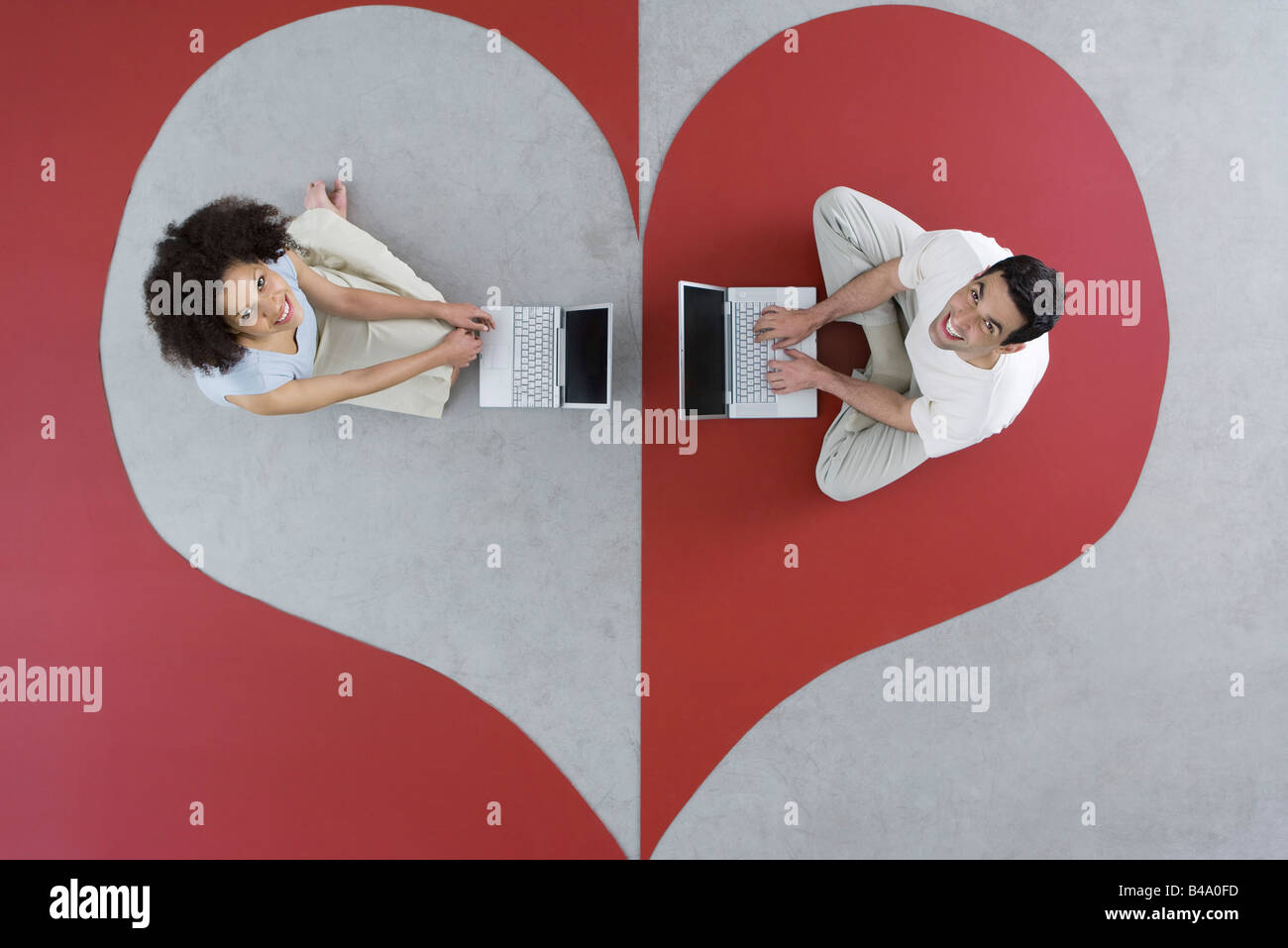 Man and woman sitting on large heart, using laptop computers, smiling ...