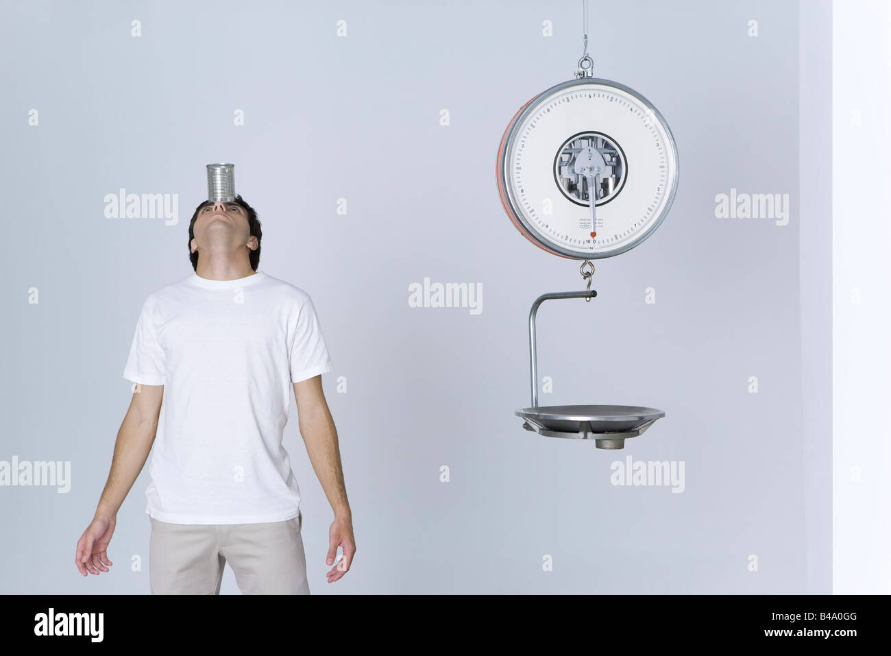 Man standing beside empty scale, balancing can on forehead Stock Photo ...
