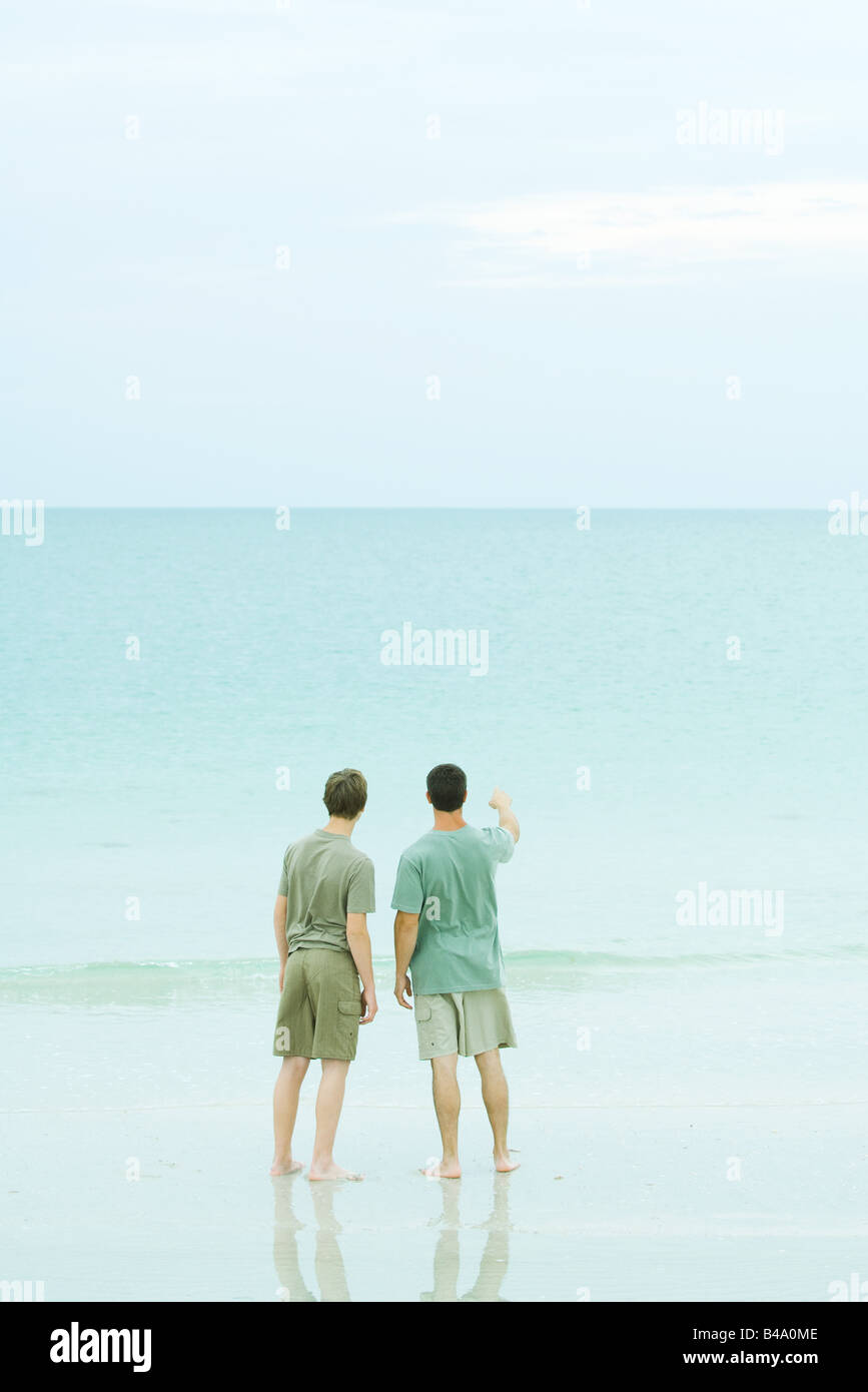 Two men standing on beach looking at the horizon Stock Photo - Alamy