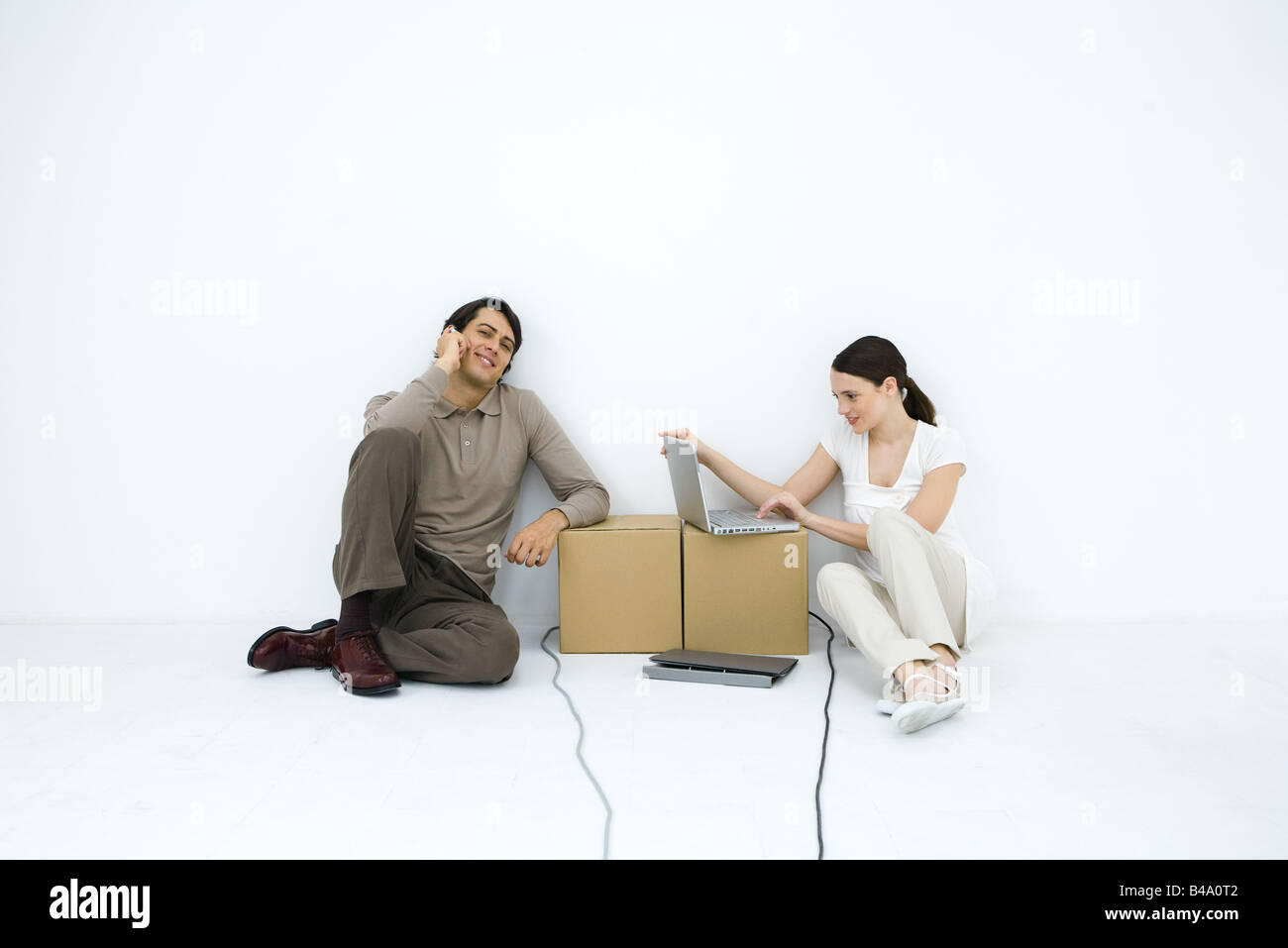 Man talking on phone, sitting on floor next to woman using laptop ...