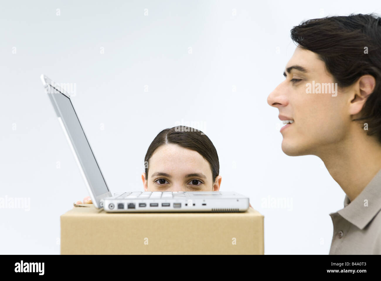 Man using laptop computer at cardboard box desk, woman hiding behind ...